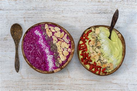 코코넛 그릇에 용 과일 아보카도 아몬드 플레이크 코코넛 칩 고 지 베리 및 치아 씨드가 들어 있는 스무디 2 개를 아침 식사와 함께 닫습니다 건강 한 식습관 슈퍼 푸드의