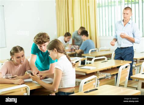 Classmates And Teacher Working In Groups To Complete Task During Class
