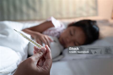 아픈 아시아 어린이 소녀는 침대에서 자고 그녀의 어머니는 집에서 침실에서 온도계와 그녀의 체온을 확인하고있다 2명에 대한 스톡 사진 및 기타 이미지 Istock