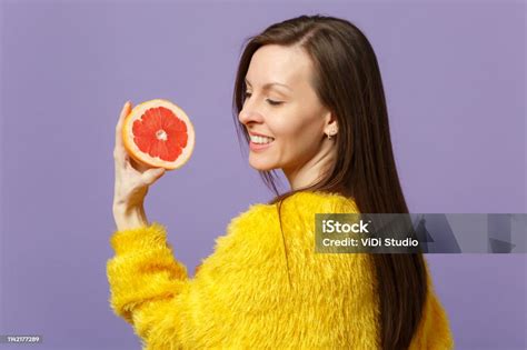 스튜디오에서 보라색 파스텔 벽 배경에 고립 된 신선한 익은 자 몽의 절반 손을 잡고 모피 스웨터에 예쁜 젊은 여자 사람들은 생생한 라이프 스타일 휴식 휴가 개념입니다 복사