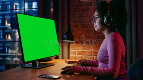 Young Beautiful Female In Headphones Working From Home On Desktop Computer With Green Screen