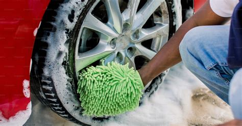 녹색 스폰지를 들고 거품으로 자동차 바퀴를 씻는 아프리카 남자의 손 야외 셀프 세차 서비스에서 고급 빨간 자동차의 현대적인 림 청소 사진 Unsplash의 세차 이미지