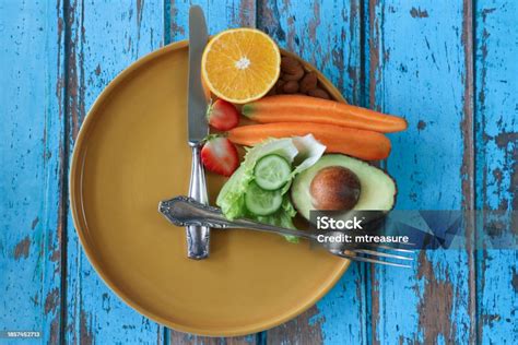 스테인레스 스틸 나이프와 포크가 있는 노란색 접시의 클로즈업 이미지 시계 문자판과 바늘 작은 섹션의 건강한 과일과 야채 청록색 파란색 나결 배경 높은 전망 복사 공간