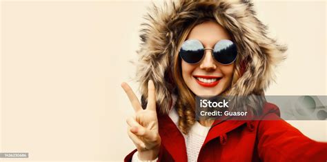 모피 후드가 달린 재킷을 입은 스마트폰으로 셀카를 찍기 위해 손을 뻗고 있는 행복한 미소 짓는 여성의 초상화 25 29세에 대한