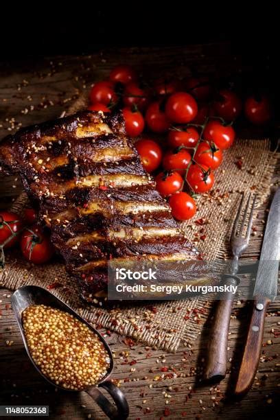 소박한 빈티지 나무 테이블 고기를 곁들인 육즙이 많은 돼지 갈비 체리 토마토 향신료 포크와 나이프 후추 로즈마리 바 질 등 어두운 배경 겨자 상단 사이드 뷰 샷 0명에 대한