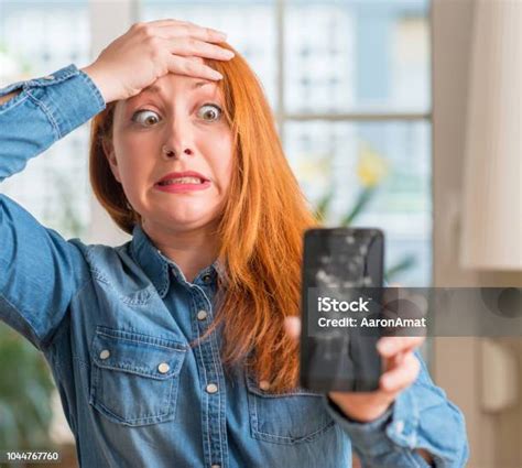 빨간 머리 여 자가 머리에 손으로 압박 깨진된 스마트폰 들고 충격 수치심과 깜짝 얼굴로 분노와 좌절 두려워 하 고 실수에 대 한 화가 깨짐에 대한 스톡 사진 및 기타 이미지