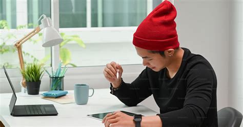 빨간 양모 모자를 쓴 젊은 남성 디자이너는 사무실에서 디지털 그래픽 태블릿과 스타일러스 펜을 가지고 책상을 작업하고 있다 사진 Unsplash의 테이블 이미지