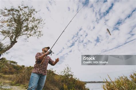 하단 보기 이루어지지 젊은이 체크 무늬 셔츠 모자 선글라스에 관목과 갈 대 근처 위치 해에서 호수에서 잡은 물고기와 낚 싯 대를 꺼내서 라이프 스타일 레크리에이션 어 부