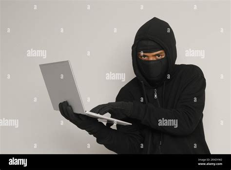 Portrait Of Mysterious Man Wearing Black Hoodie And Mask Doing Hacking Activity On Laptop