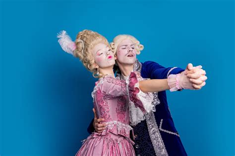 바로크 양식의 의상을 입은 우아한 커플이 생생한 푸른 배경에 즐거운 귀족 춤을 보여줍니다 16 17 살에 대한 스톡 사진 및