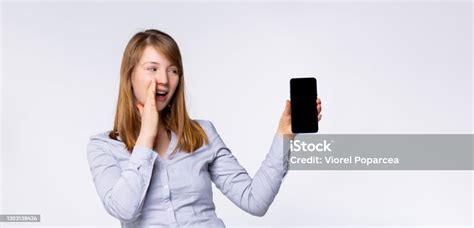 배너 긴 형식 흥분 한 여자는 비명을 지르고 회색 배경에 고립 된 빈 검은 색 빈 화면으로 휴대 전화를 잡습니다 사람들은 진지한 감정 라이프 스타일 광고 복사 공간을