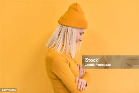 금발 머리 여자의 측면 보기 착용 노란색 옷 모자 노란색 스튜디오 배경에서 포즈 광고 또는 프로 모션에 대 한 공간을 복사 합니다 백인 여성 내려다보고 하 고 그녀의 손에