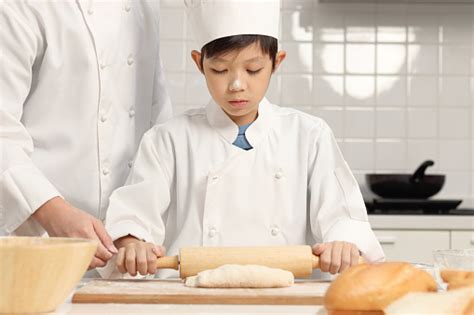 모자를 쓴 셰프 유니폼을 입은 행복한 아시아인 아들과 아버지는 부엌에서 함께 식사를 요리하고 귀여운 소년은 밀대로 반죽을 반죽하고 부모와 아이는 빵집을 만든다 어린이 학생은