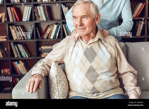 Father And Babe At Home Library Woman Doing Massage To Senior Man Sitting On Sofa Thoughtful