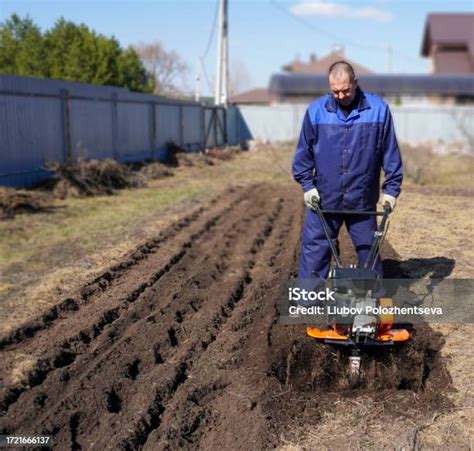 한 남자가 이른 봄에 채소밭에서 일합니다 땅을 파다 경운기 보행형 트랙터로 작동합니다 경작지에 대한 스톡 사진 및 기타 이미지
