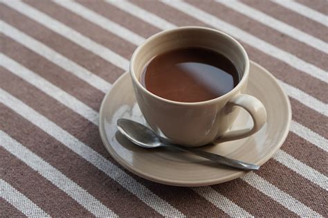 갈색과 흰색 패브릭 배경에 크림 세라믹 컵에 담긴 뜨거운 갈색 커피와 크림 세라믹 코스터에 있는 은색 숟가락 음료 음식 건강 복사 공간 갈색에 대한 스톡 사진 및 기타