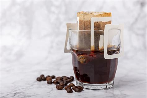 커피 백 커피 원두 유리 컵을 텍스처 테이블에 떨어 뜨립니다 컵에 양조하기 위한 분쇄 커피 종이 봉지 드립 커피 필터 포장 복사할 장소 텍스트를 위한 위치입니다 0명에 대한