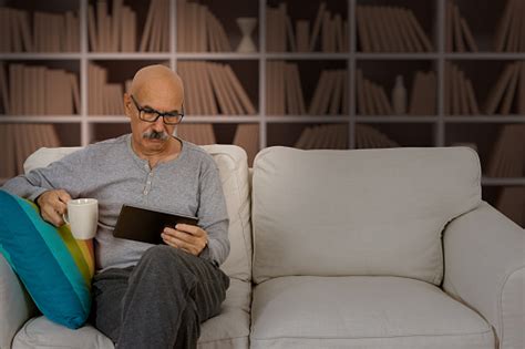 하우스 거실에서 소파에 앉아 디지털 태블릿에서 선임 남성 독서 60 64세에 대한 스톡 사진 및 기타 이미지 60 64세 가정 생활 거실 Istock