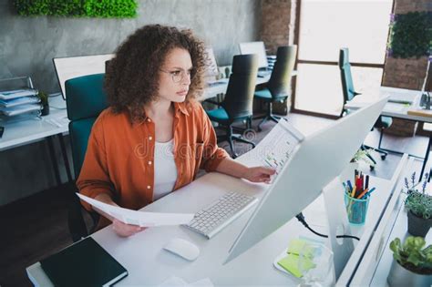 Focused Young Businesswoman Reviewing Documents And Working At A Computer In A Bright Modern