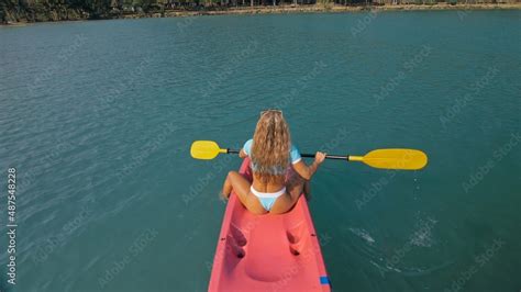 Seductive Sexy Blonde Woman In Blue Swimsuit Sails On Pink Plastic Kayak Along Azure Sea At