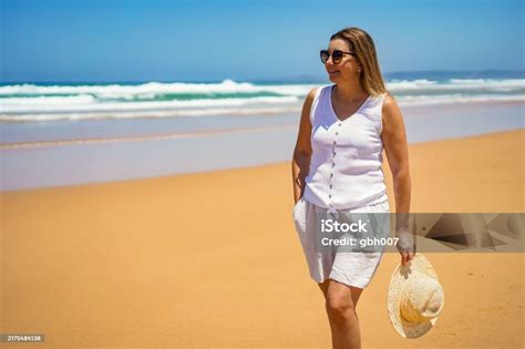 더운 날씨에 가벼운 옷을 입고 여름날 모래 사장을 걷는 태양 모자와 선글라스를 쓴 중반 성인 아름 다운 여성 보르데이라 프라이아 포르투갈 해변에서 휴식을 취하고 차분하게