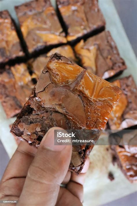 기름을 자른 양피지 베이킹 페이퍼 갈색 질감배경 높은 시야위에 수제 초콜릿 소금에 절인 캐러멜 브라우니의 사각 조각을 들고 있는 인식할 수 없는 사람의 이미지 갈색에 대한