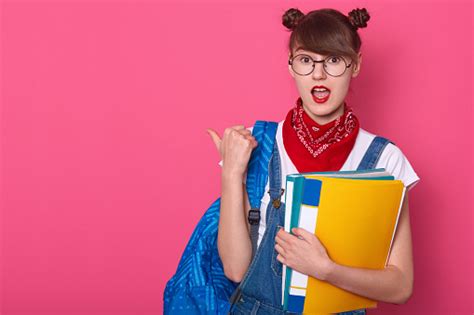 즐거운 머리 만두를 가지고 노란색 폴더를 들고 흰색 티셔츠 데님 바지 빨간 반다나 안경 어깨에 파란색 배낭을 들고 즐거운 Apearance와 여자의 수평 샷 T 셔츠에 대한