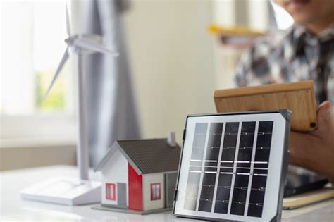 엔지니어의 책상 위에는 태양 전지판 설치에서 가장 비용 효율적인 에너지를 얻기 위해 집에 태양 전지판 설치를 계획하는 데 사용할 집과 태양 전지판의 모형이 놓여 있습니다