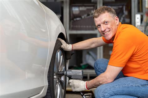 자동차 수리점에서 자동차의 공압 렌치 변하는 타이어를 사용하는 남성 정비사 볼트를 풀어주는 전기 드릴로 자동차의 전문 정비사 검사 수리 및 유지 보수 휠 50 54세에 대한