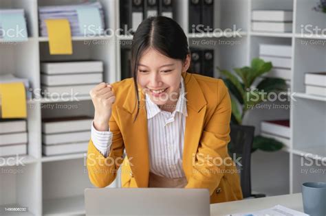 노란 양복을 입은 젊은 아시아 사업가가 노트북과 스마트폰을 통해 동료들에게 기쁨을 보여주며 성공의 개념인 정해진 목표를 가진 회사 프로젝트를 완수했다 가상현실에 대한 스톡