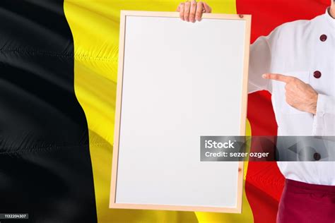 벨기에 국기 배경에 빈 화이트 보드 메뉴를 들고 벨기에 요리사 텍스트에 대 한 균일 한 포인팅 공간을 착용 요리 고급 요리에 대한 스톡 사진 및 기타 이미지 Istock