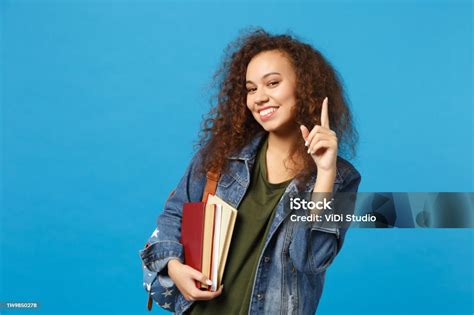 데님 옷에 젊은 아프리카계 미국인 소녀 사춘기 학생 배낭은 파란색 벽 배경 스튜디오 초상화에 고립 된 책을 잡아 고등학교 대학 대학 개념에서 교육 복사 공간을 모의 가방에