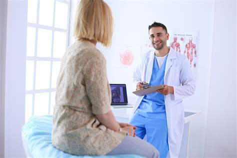 잘생긴 의사는 젊은 여성 환자와 얘기 하 고 그의 사무실에 앉아있는 동안 메모를 만들기 개념에 대한 스톡 사진 및 기타 이미지 개념 개념과 주제 건강관리와 의술