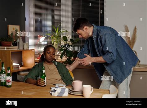 Young Worried Husband Bending Over Depressed Wife With Bottle Of Beer