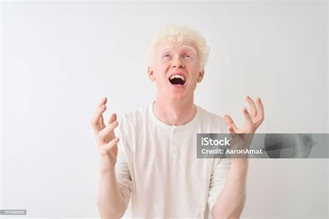 젊은 알비노 금발 남자는 고립 된 흰색 배경 에 서 캐주얼 티셔츠를 입고 미친 미친 소리와 공격적인 표정과 팔을 제기 와 고함