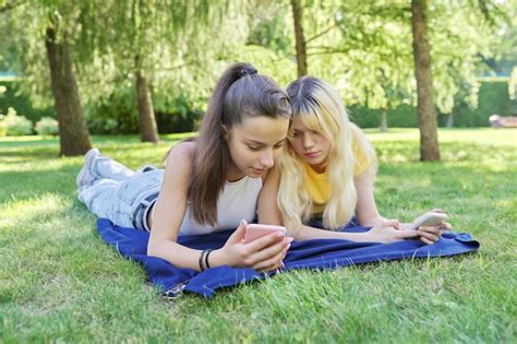 Premium Photo Two Young Female Teenagers Lying On Grass In Park With