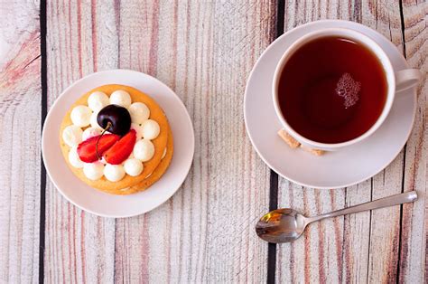 크림 체리 딸기를 곁들인 스폰지 꿀 케이크는 차 한 잔 옆에 있는 나무 테이블에 서 있습니다 과일에 대한 스톡 사진 및 기타