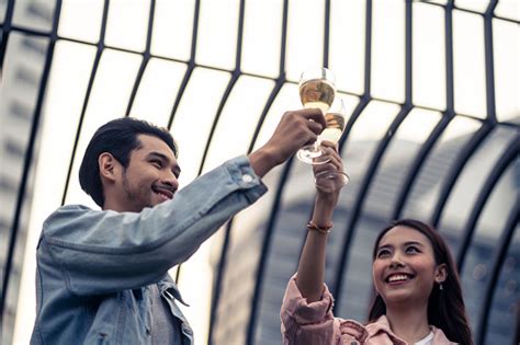옥상에서 함께 기념일 파티를 축하하는 아시아 젊은 부부 화이트 와인 토스트 한 잔을 들고 행복과 미소로 마시는 남자와 여자 어린 소년과 소녀 개념의 사랑 20 24세에 대한