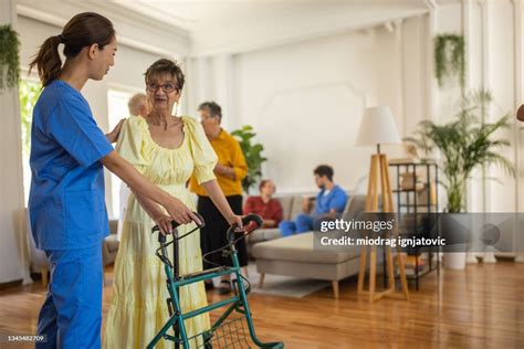 Nurse Assisting Senior Woman To Walk With Mobility Walker In Nursing
