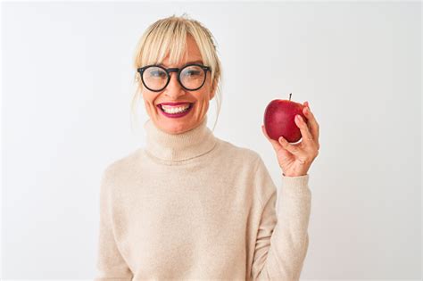 고립된 흰색 배경 위에 사과서를 들고 있는 중년 여성이 행복한 얼굴을 하고 이빨을 보여주는 자신감 넘치는 미소를 지으며 미소짓고 있습니다 건강한 생활방식에 대한 스톡 사진