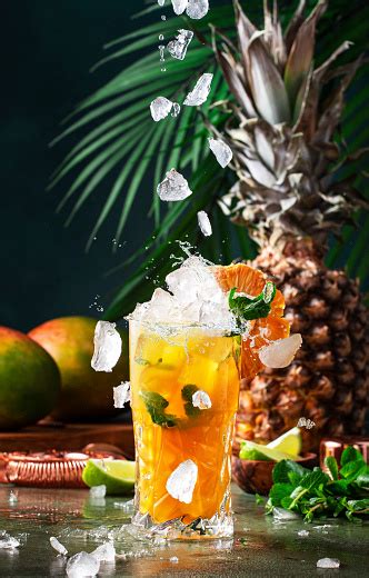 보드카 파인애플 주스 망고 얼음을 곁들인 여름 칵테일 긴 음료 또는 차가운 목테일 분쇄 된 얼음이 유리에 튀어 나오고 얼어 붙은 움직임과 날아 다니는 방울이 쏟아집니다