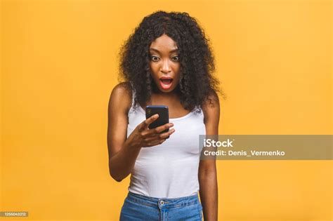 그녀의 초상화는 노란 배경을 통해 고립 된 웹에서 채팅 손 전화에 들고 쾌활한 쾌활한 쾌활한 물결 모양의 아프리카 계 미국인 흑인 소녀를 집중 사랑스러운 Winsome 을