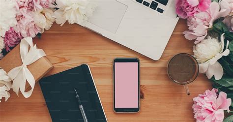 빈 화면 노트북 커피 컵 노트북 테이블에 분홍색과 흰색 모란이 있는 선물이 있는 세련된 전화기는 텍스트를 위한 공간이 있습니다 프리랜서 개념입니다 세련된 작업