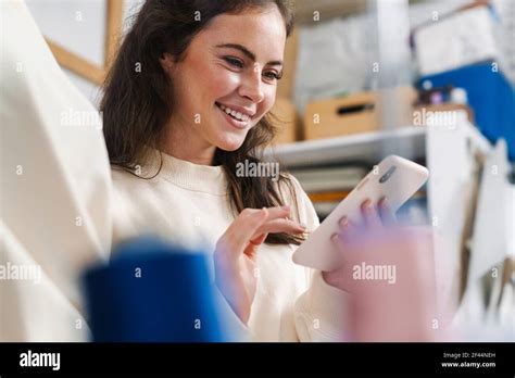 Smiling Nice Brunette Girl Seamstress Using Mobile Phone While Working