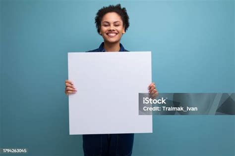 검은 피부와 검은 곱슬 머리를 가진 젊은 성공한 여성이 프로젝트 쇼케이스에 대 한 흰색 빈 포스터를 들고 파란색 데님 정장을 입고 쥠에 대한 스톡 사진 및 기타 이미지