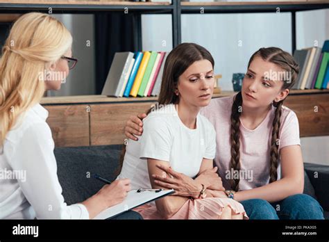 Female Counselor Writing In Clipboard While Daughter Embracing