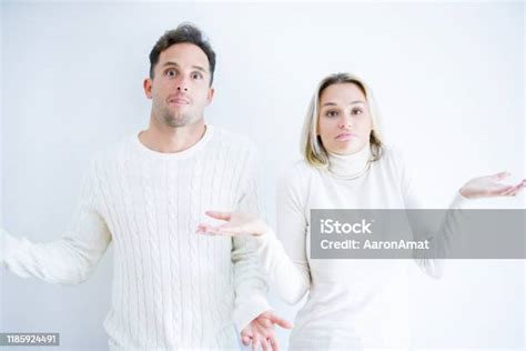 고립 된 흰색 배경 에 서 캐주얼 티셔츠를 입고 젊은 아름다운 부부는 팔과 손을 들고 단서와 혼란 스러운 표정 의심 개념 2명에