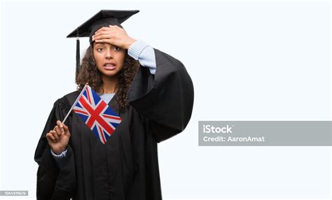 젊은 스페인 여자 입고 졸업 유니폼 들고 깃발 영국 손으로 머리 수치심과 놀라움으로 충격된에 스트레스의 얼굴 분노와 좌절 두려워 하 고 실수에 대 한 화가 감정에 대한 스톡