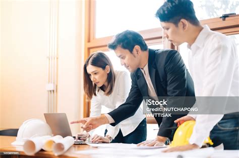 3명의 남성과 여성으로 구성된 아시아 건축 팀이 사무실에서 노트북 엔지니어링 프로젝트 설계 건설 산업 사업 계획에 대해 함께 일하고 있습니다 청사진과 헬멧이 있습니다