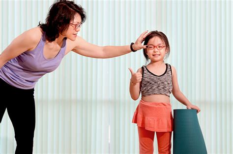 실내 스튜디오에서 요가 운동을하는 어머니와 딸 함께 서서 요가를 연습하는 스포티 한 가족 요가 매트를 들고 서서 엄지 손가락을 올리는 귀여운 아이 아이의 머리를 쓰다듬는